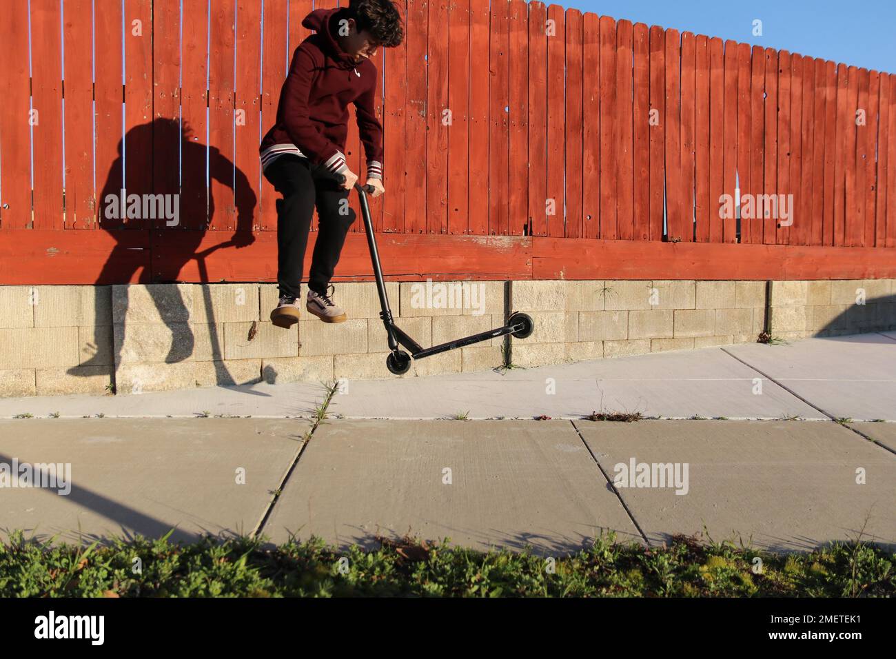 A young male doing a trick on a scooter near a wooden fence Stock Photo ...
