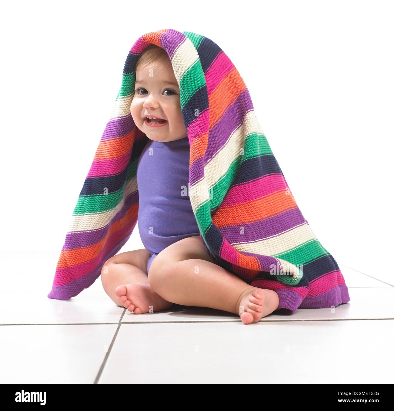 Baby girl (12 months) with colourful striped blanket on her head Stock ...