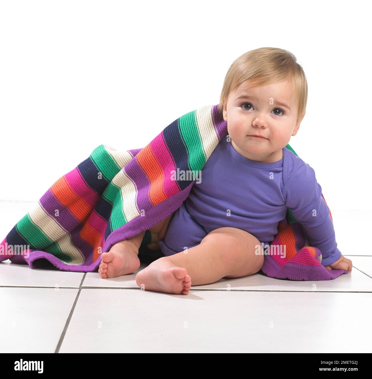 Baby girl (12 months) with colourful striped blanket over her shoulder ...