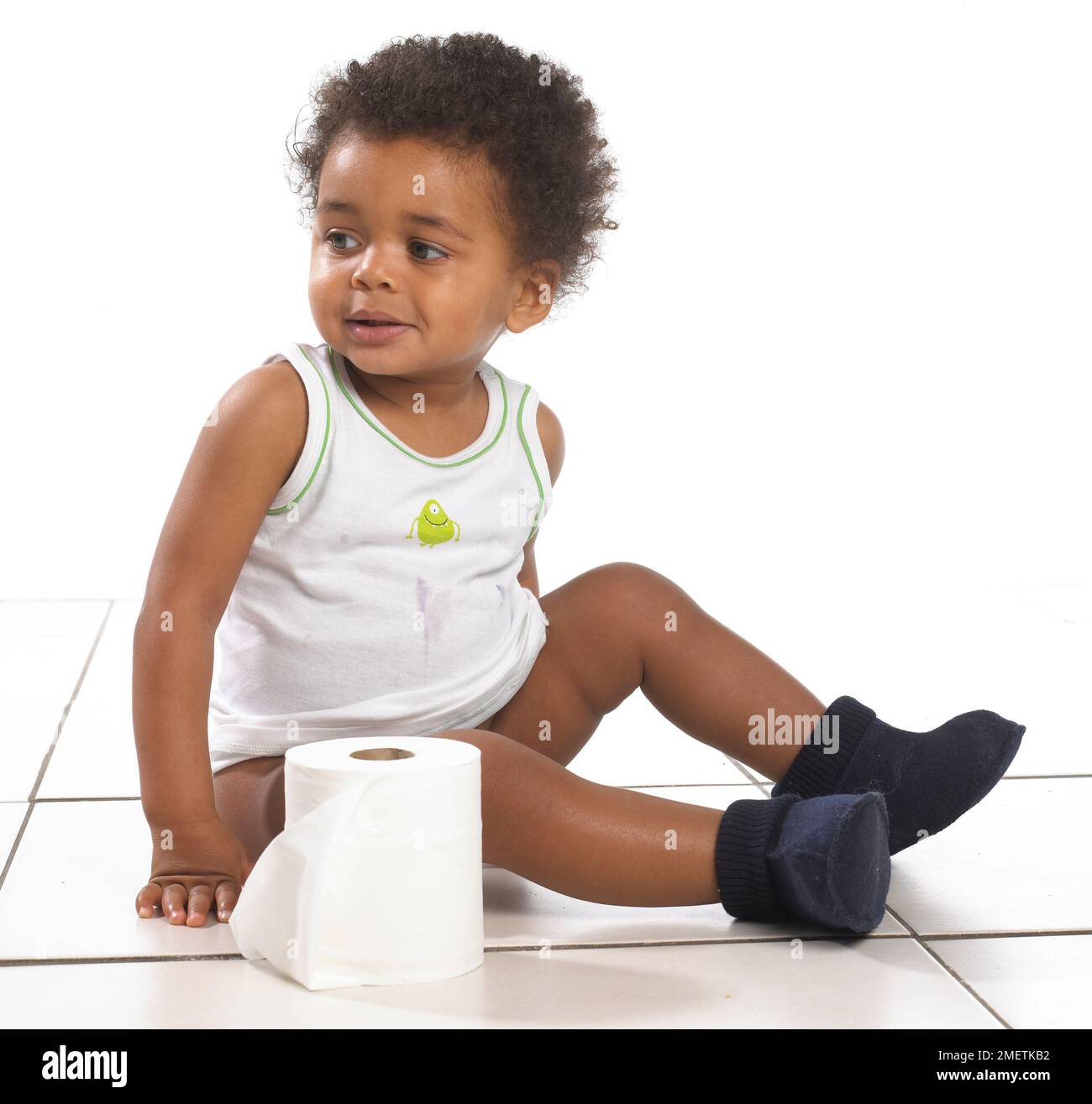 Boy wearing vest and slippers sitting on floor with roll of toilet ...