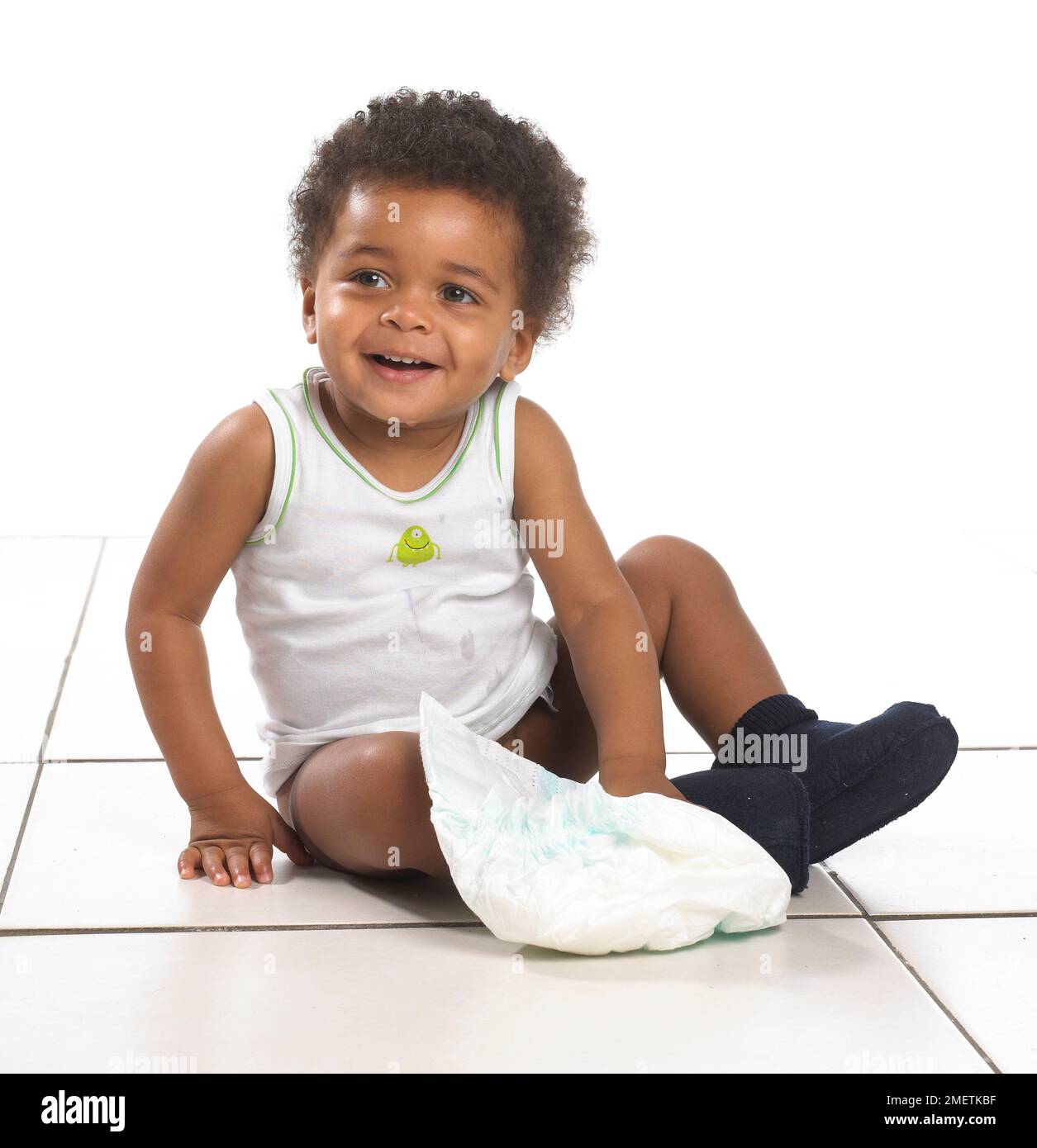 Boy wearing vest and slippers sitting on floor, with nappy, 17 months ...