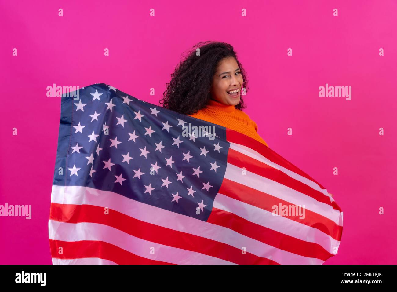 Curly-haired woman with the usa flag on a pink background, studio shot ...