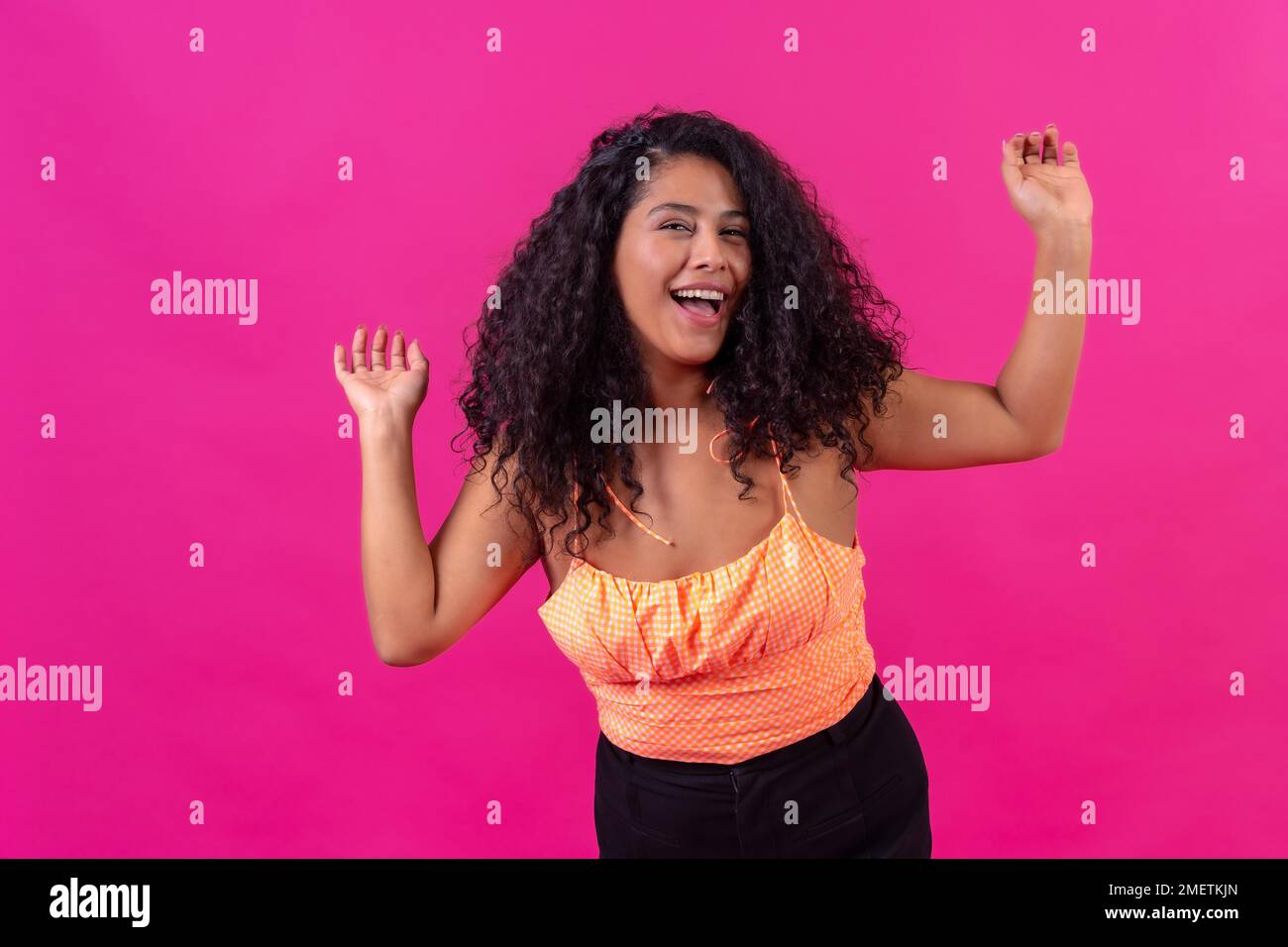 Curly-haired woman in summer clothes on a pink background dancing ...