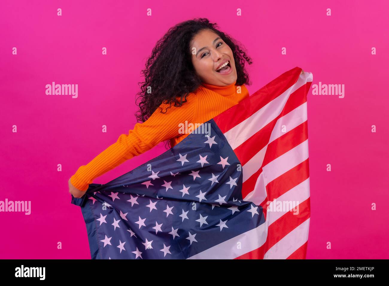 Curly-haired woman with the usa flag on a pink background, studio shot ...