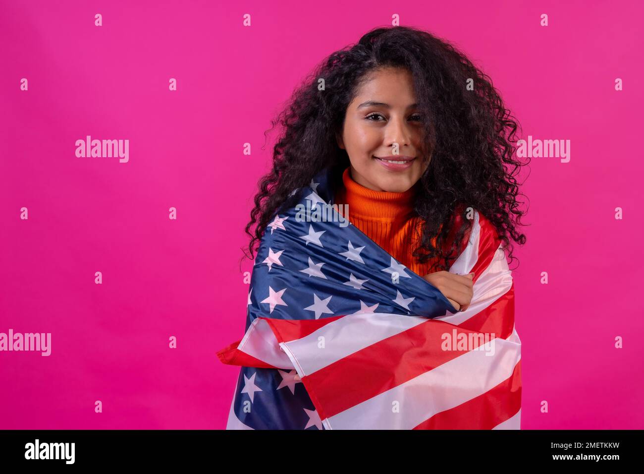 Portrait of a curly-haired woman smiling with the usa flag on a pink ...