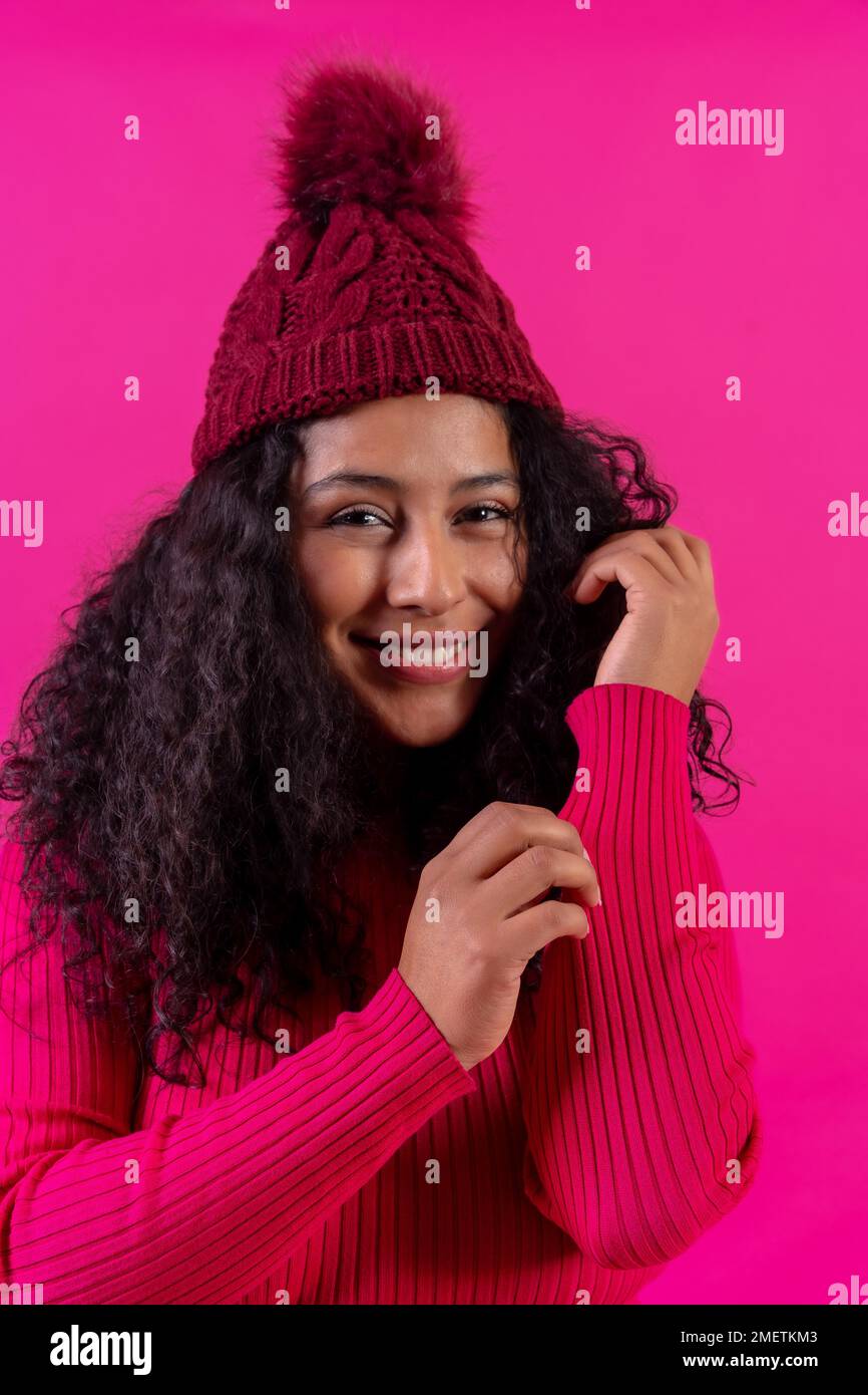 Curly-haired woman in a wool cap on a pink background portrait smiling ...