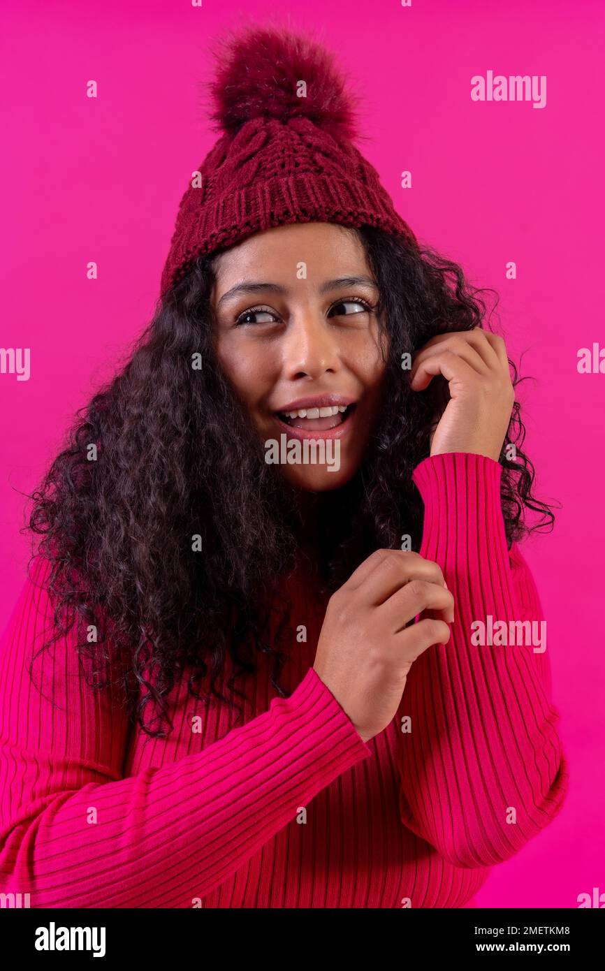 Curly-haired woman in a wool cap on a pink background portrait smiling ...
