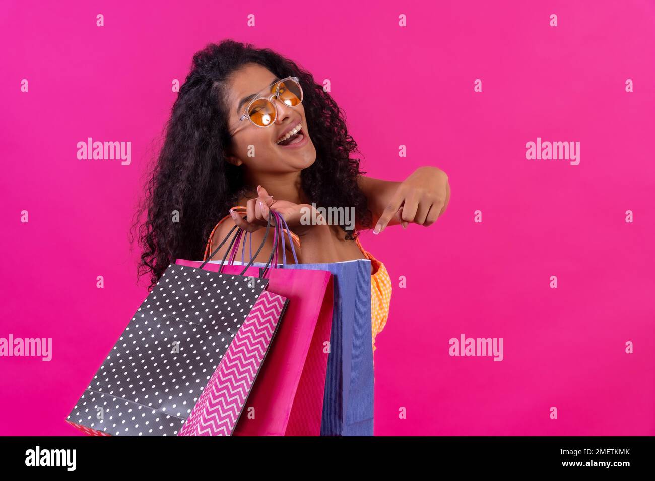 Curly-haired woman on a pink background, shopping concept, pointing at ...