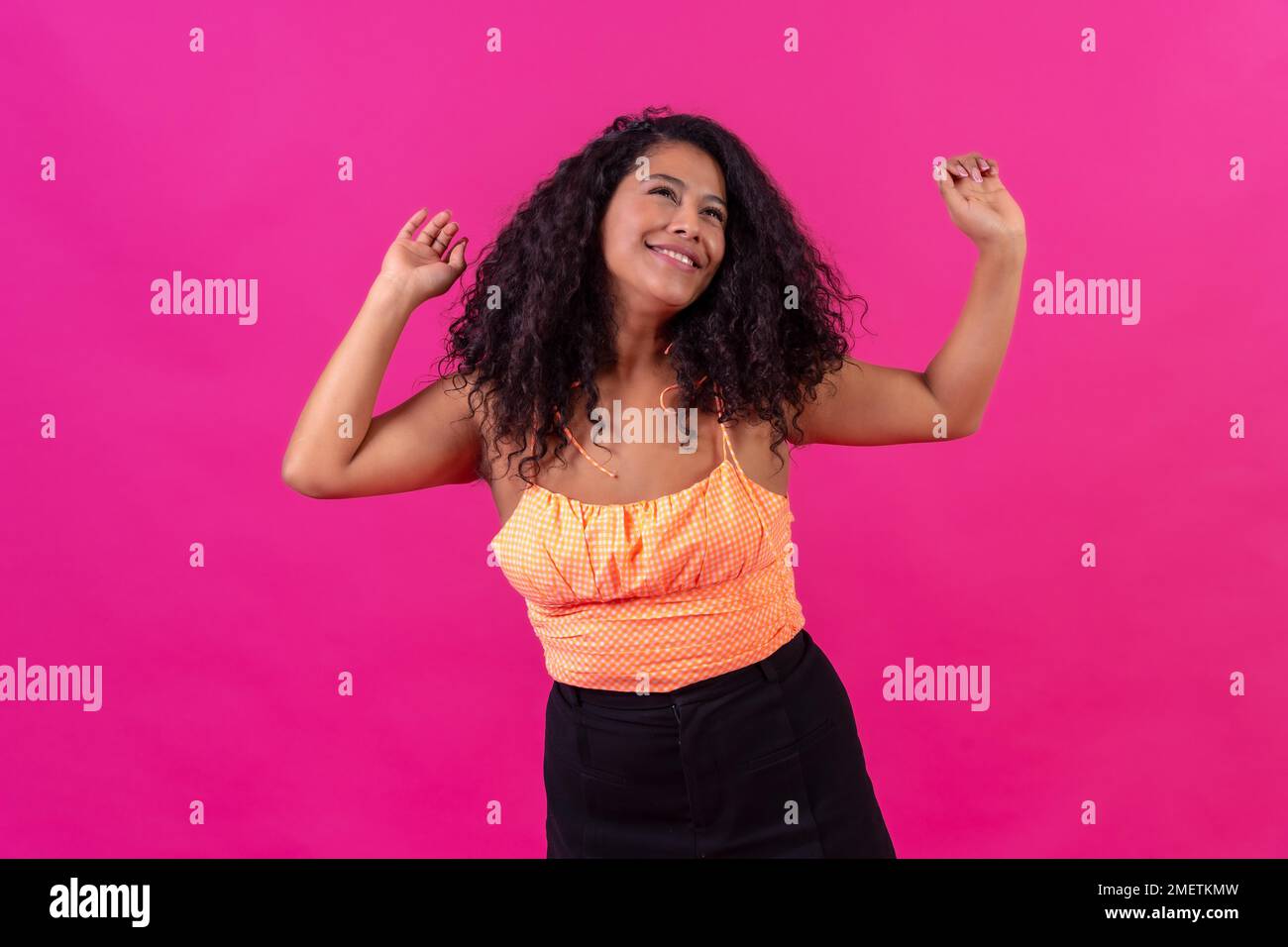 Curly-haired woman in summer clothes on a pink background dancing ...