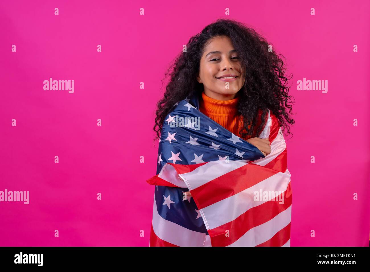 Portrait of a curly-haired woman smiling with the usa flag on a pink ...