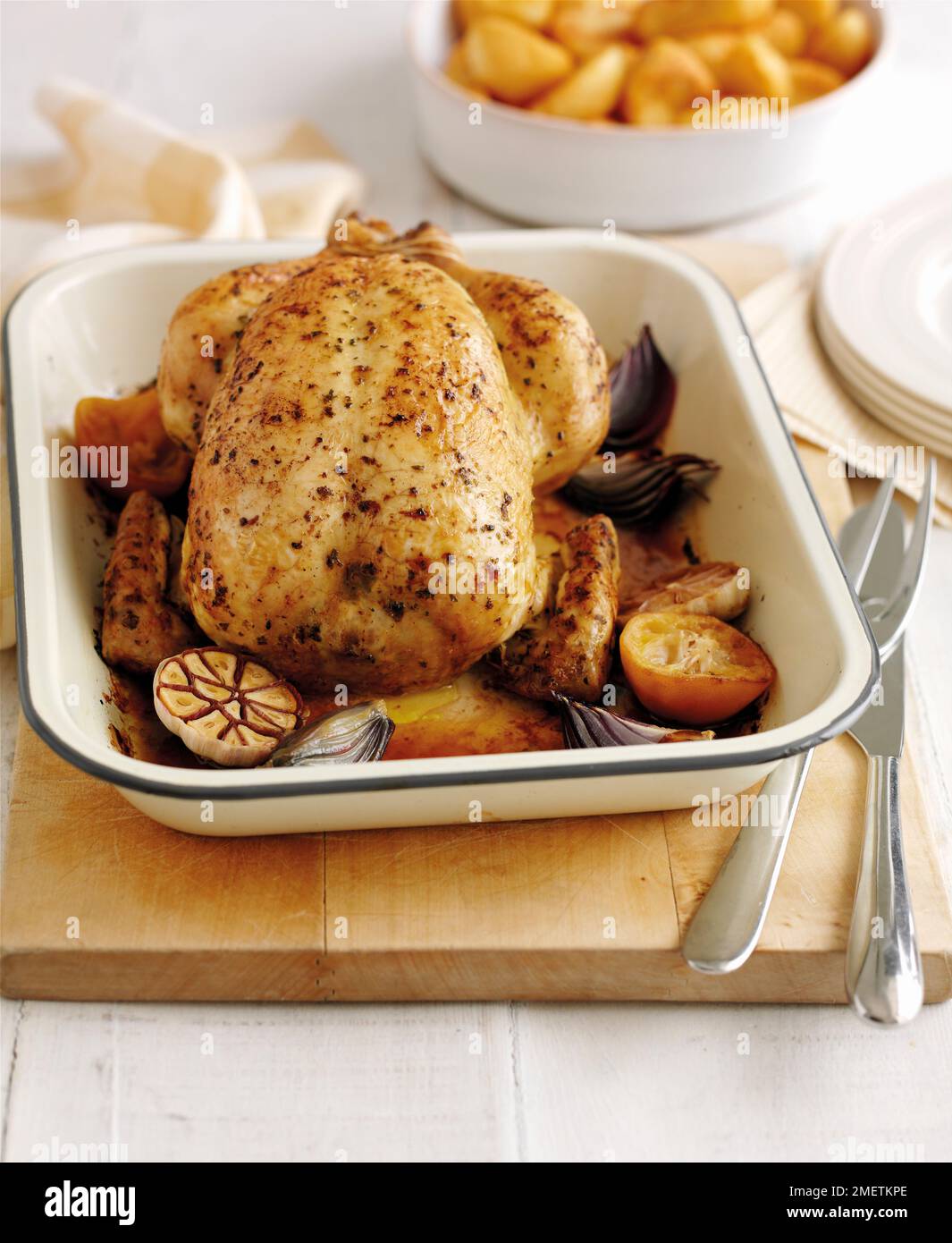 Roast chicken basted in herb butter, in roasting tin with garlic ...