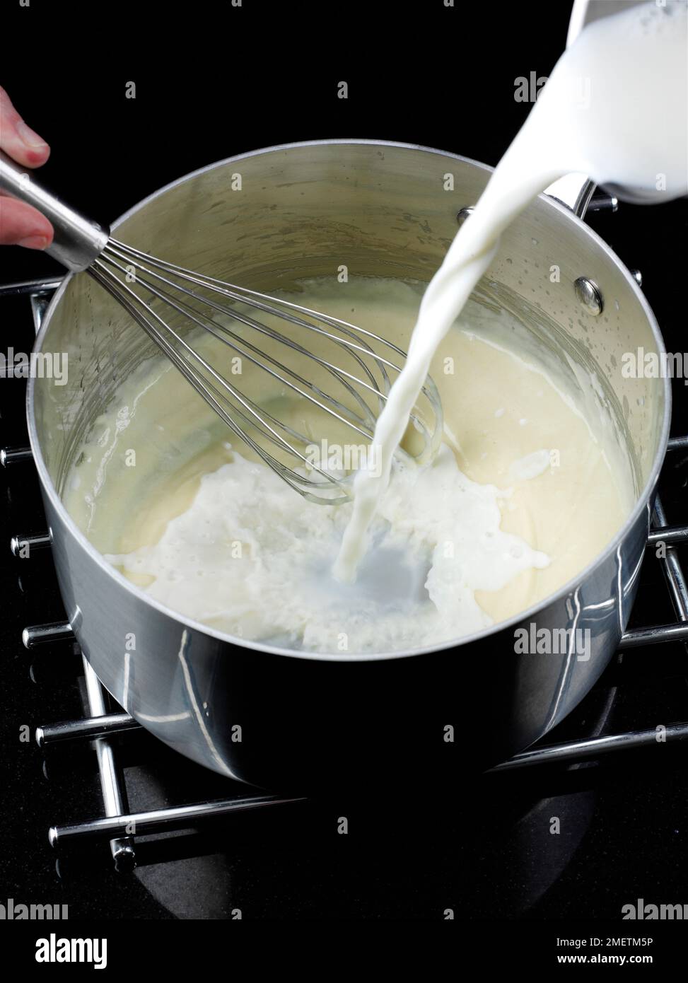 Making cheese souffles, pouring milk into butter and flour mixture and ...