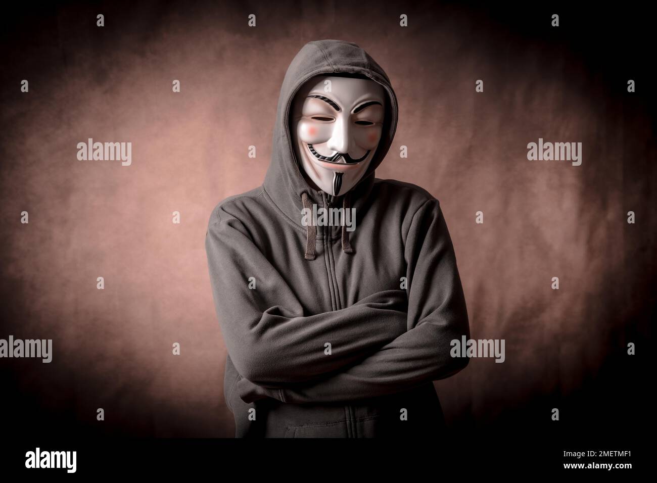 Man wearing anonymous mask with sweatshirt, looking down, studio shot ...