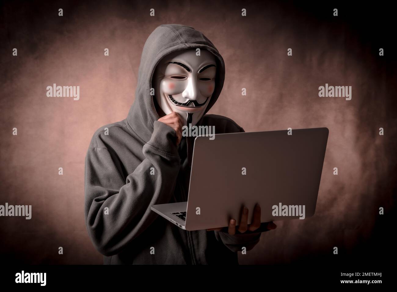 Hacker with anonymous mask with a laptop thinking about programming ...