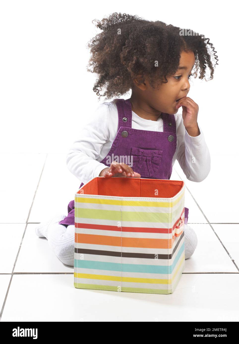 Girl kneeling next to colourful stripy box, 3 years Stock Photo - Alamy