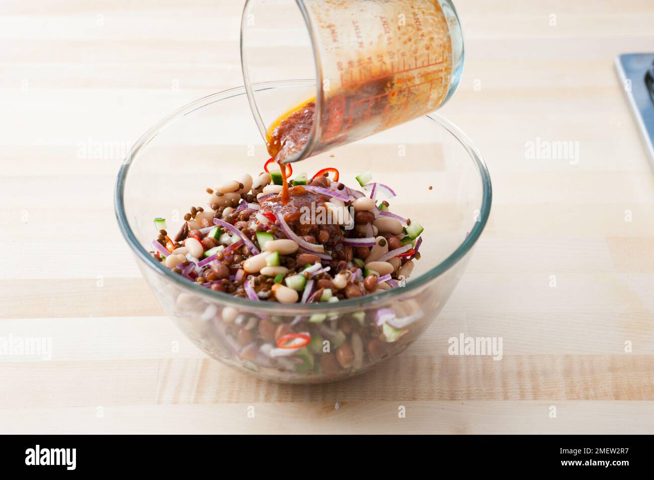 Making lentil and chilli bean salad, mixing in harissa dressing Stock ...