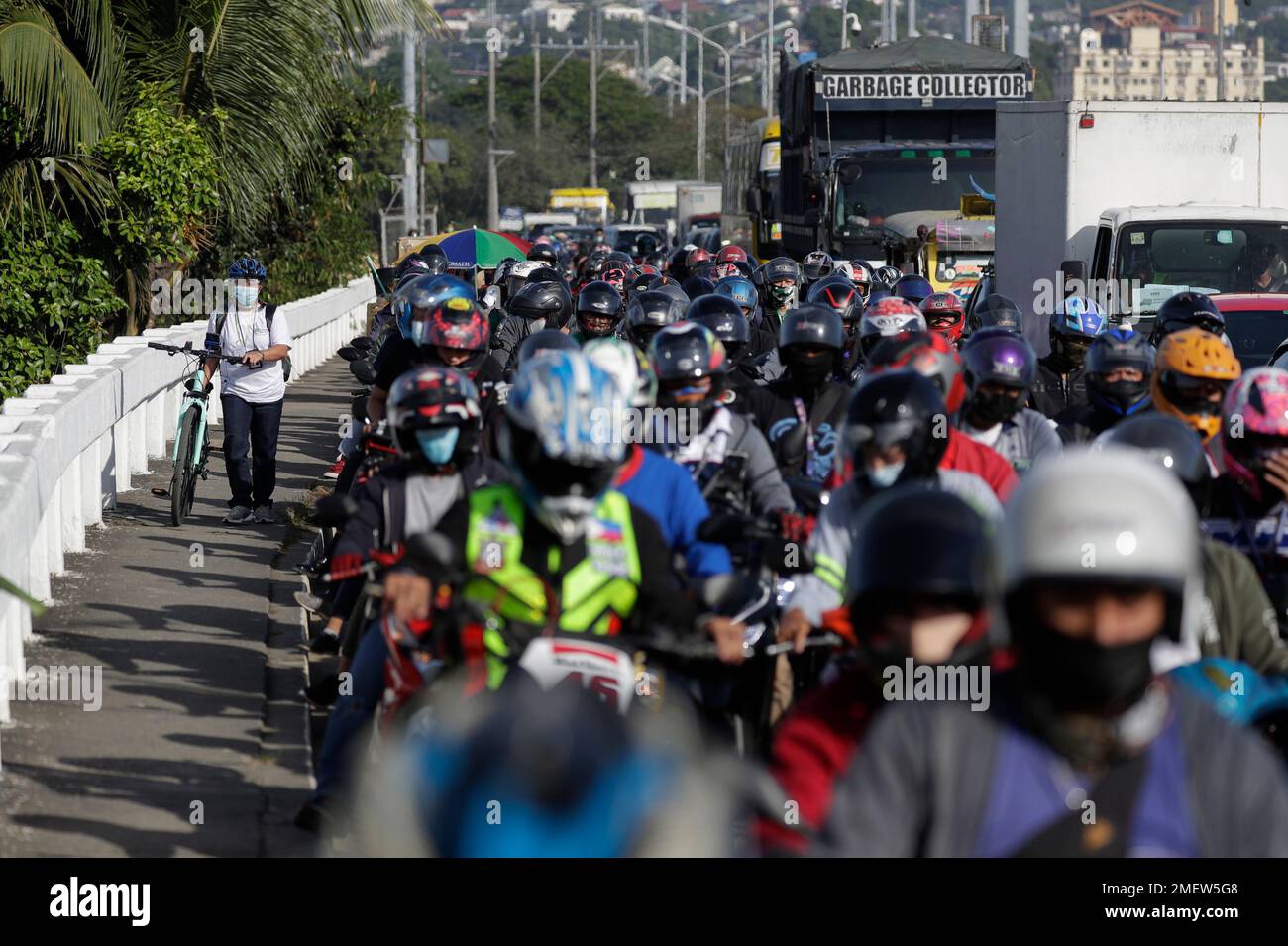 A woman pushes her bicycle beside a crowd of motorcycle riders at a ...