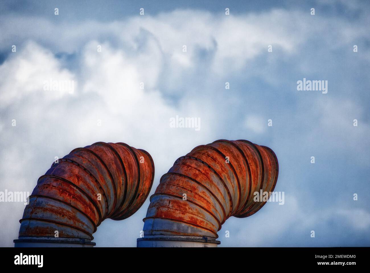 Rusty industrial air vents against a blue sky and fluffy cloud backdrop ...