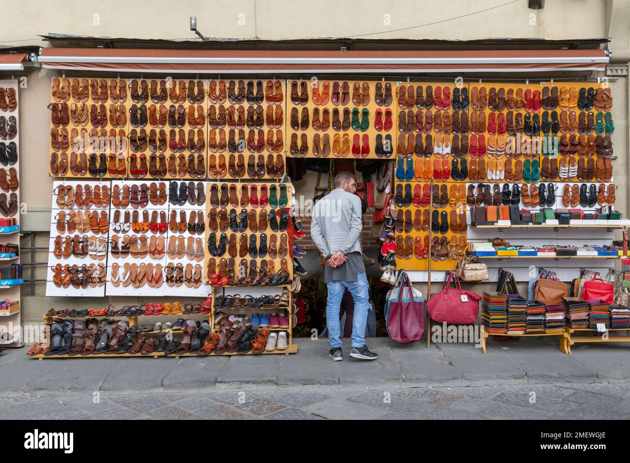 Salesman standing outside of leather shop with assortment of leather ...