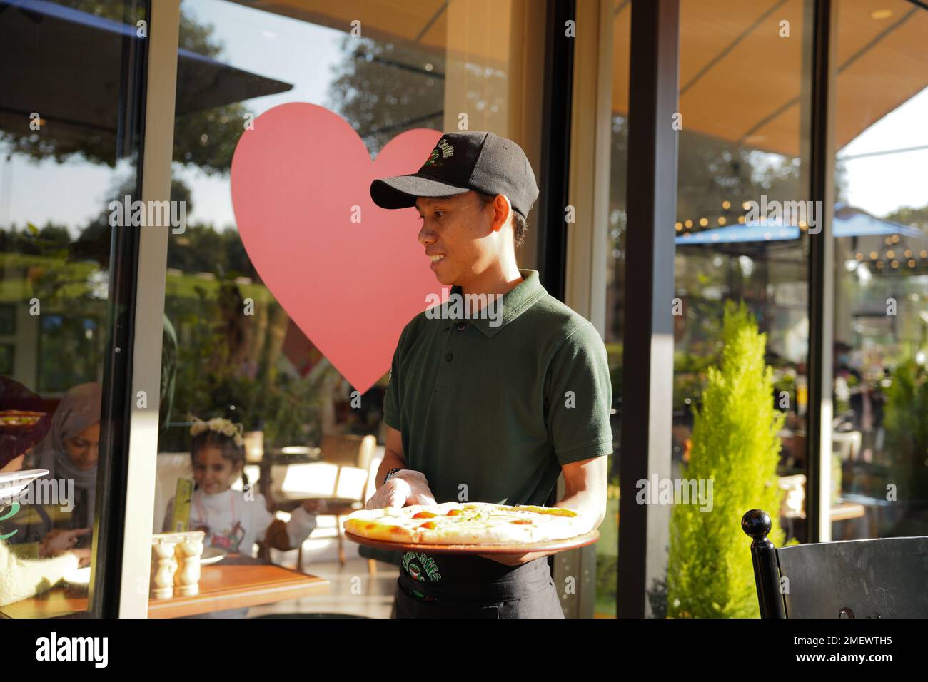 Restaurant staff holding a customer ordering a pizza on a sunny day ...