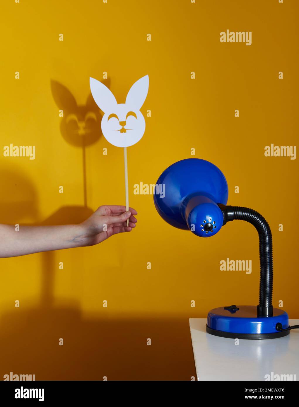 Blue table lamp casting a shadow of a rabbit mask on a yellow ...