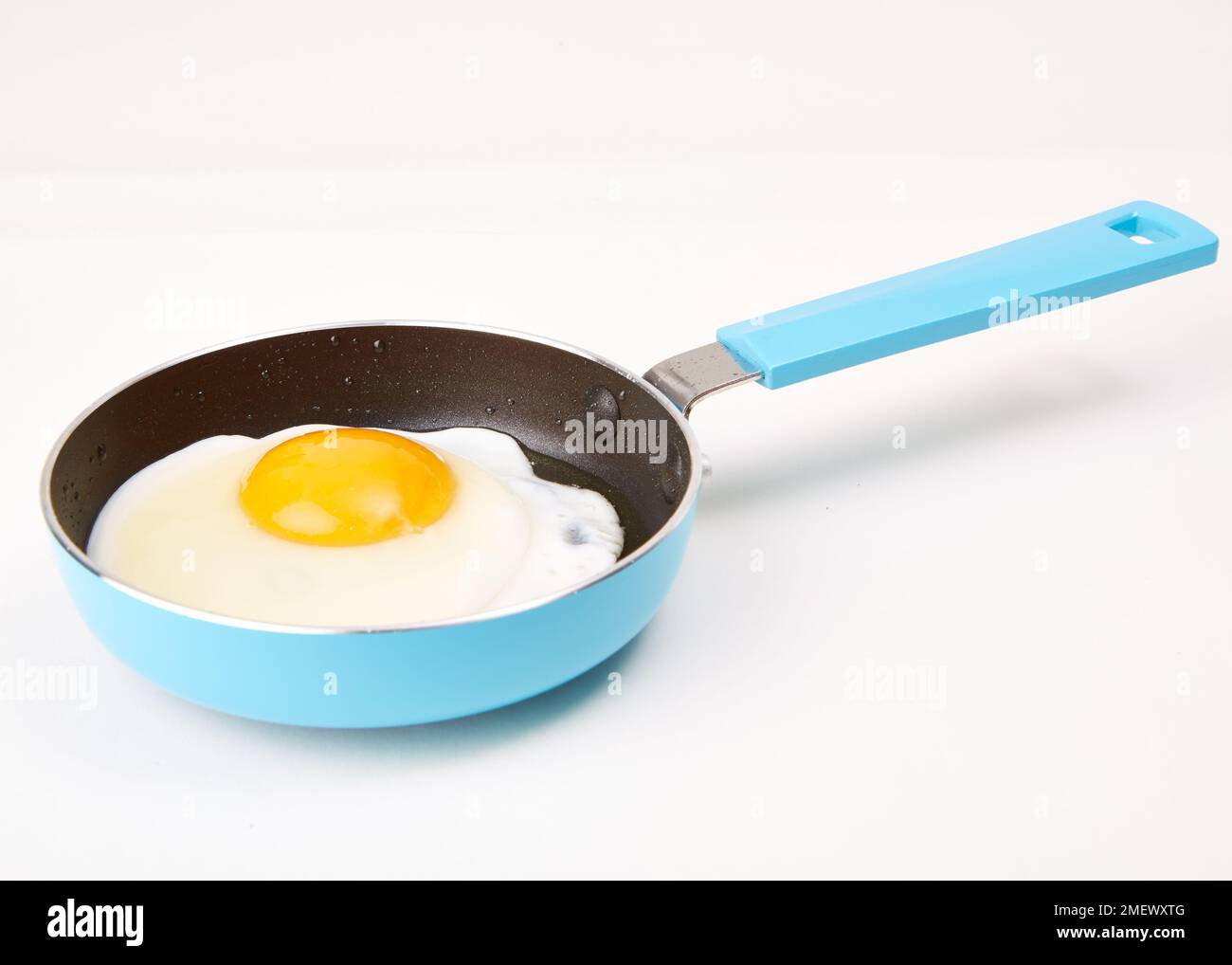 Egg being cooked in blue frying pan Stock Photo - Alamy