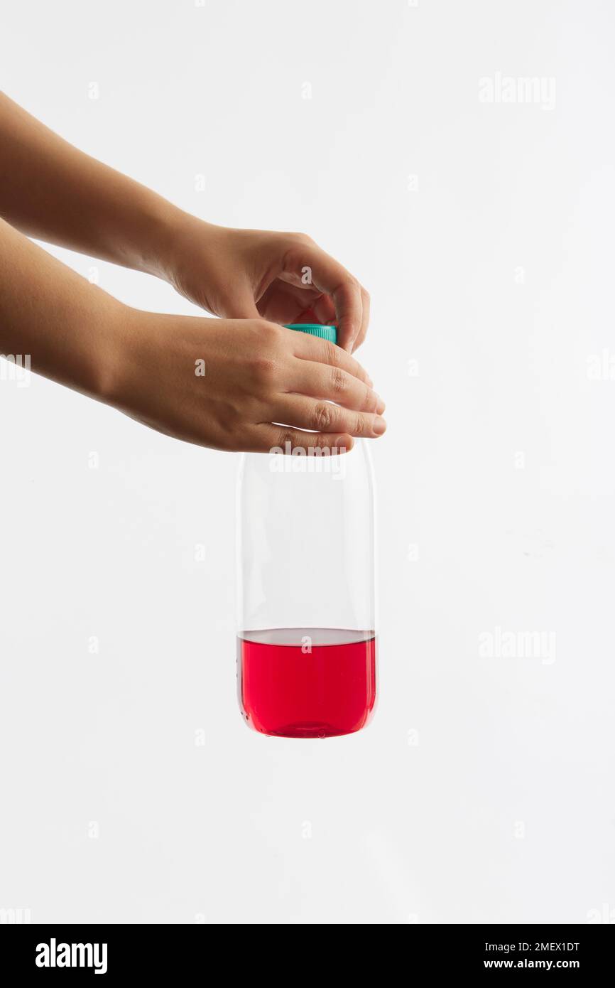Plastic bottle of red liquid held in two hands Stock Photo - Alamy