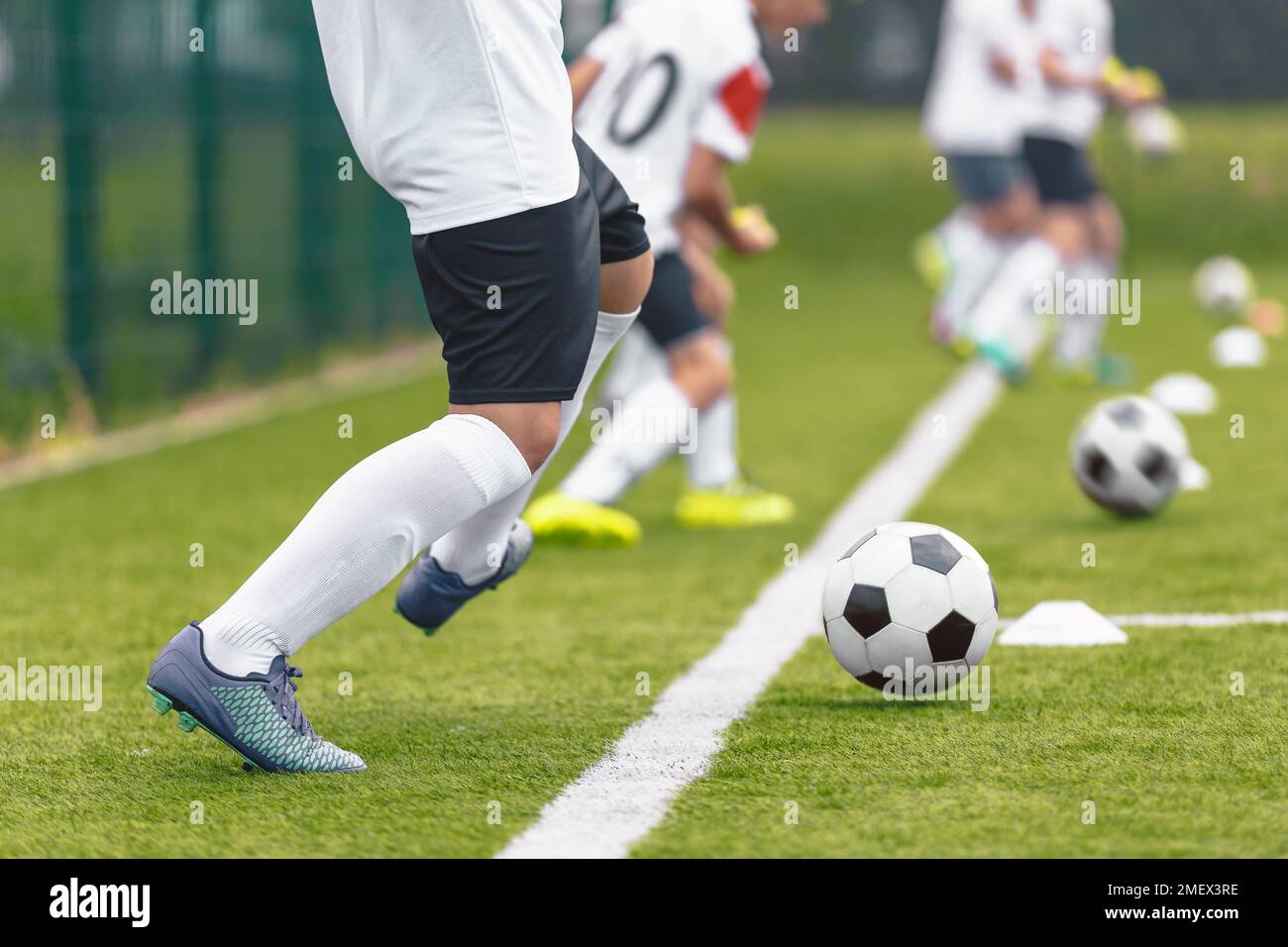 Group of soccer players kicking balls on training drill along sideline ...