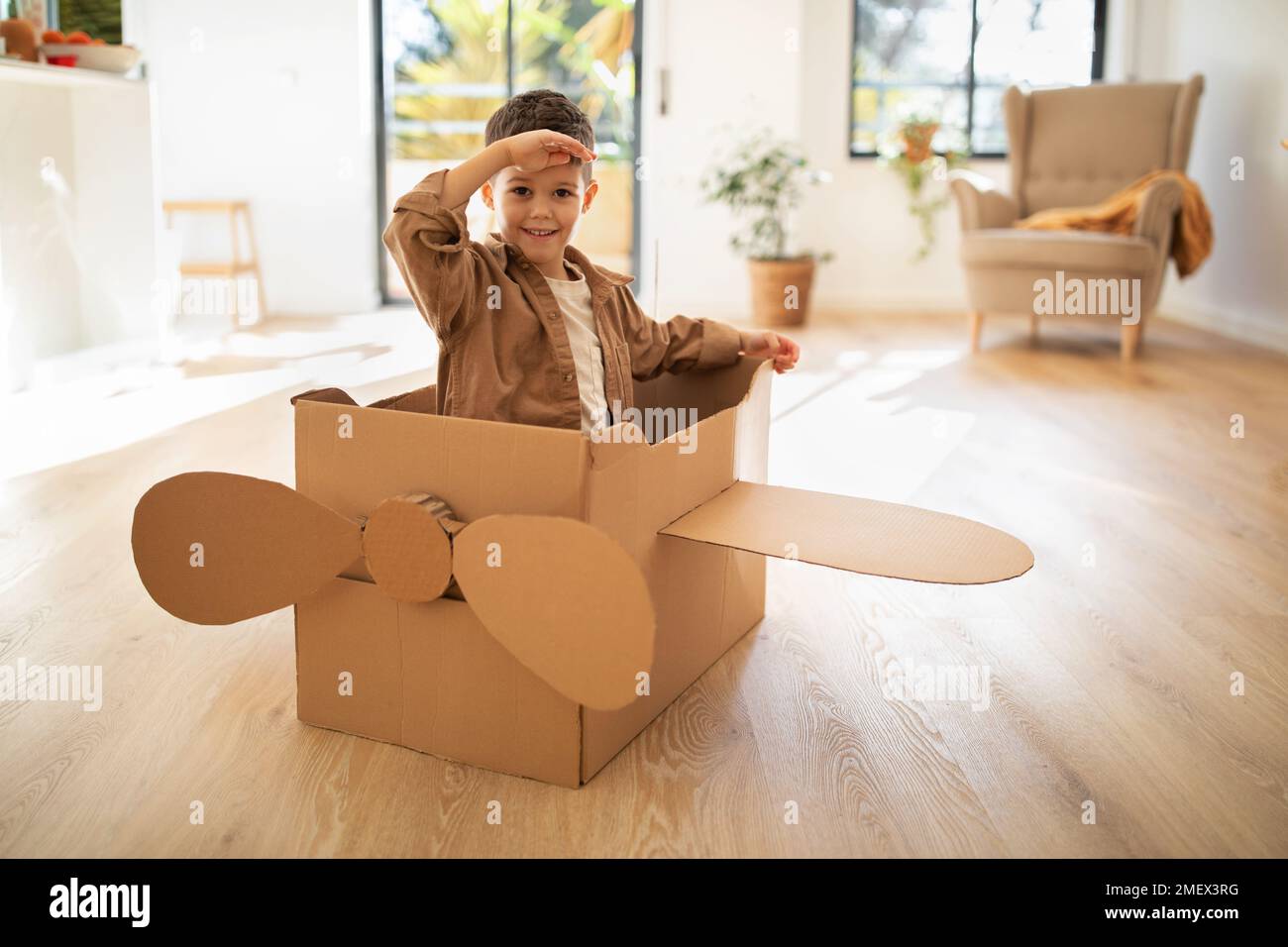 Smiling little european boy in cardboard box helicopter looks at ...