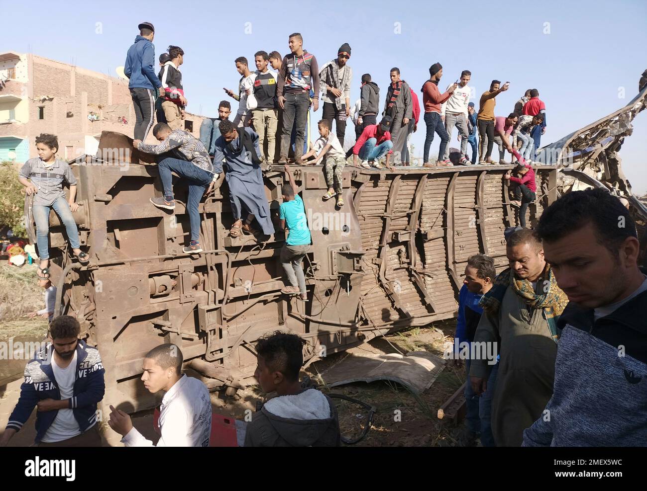 Egyptians gather around mangled train carriages at the scene of a train ...