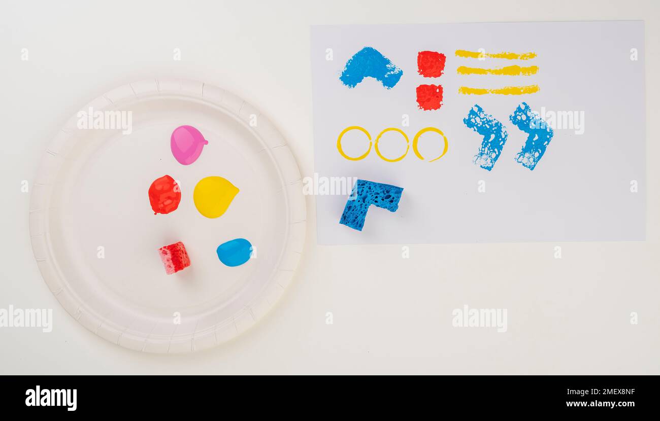 Paper plate with coloured paint and sponges testing shapes on paper ...