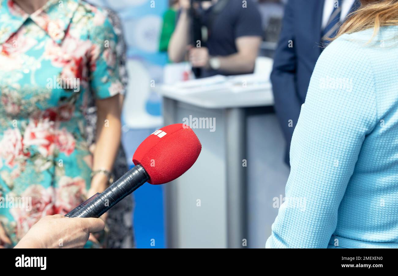 Journalist at news conference holding microphone making media interview with female politician ...