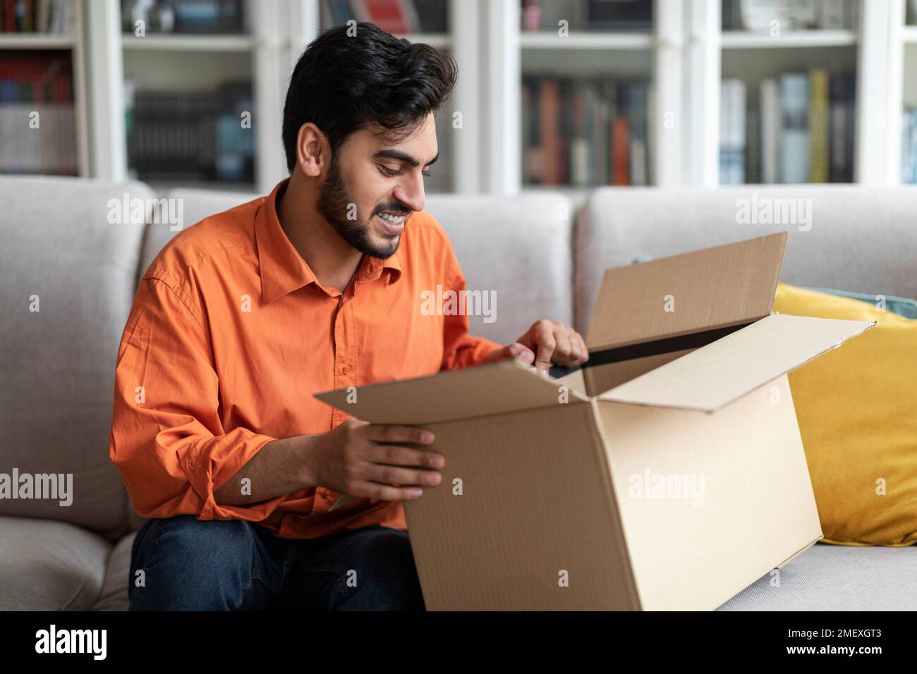 Smiling middle eastern man customer opening good parcel, home interior ...