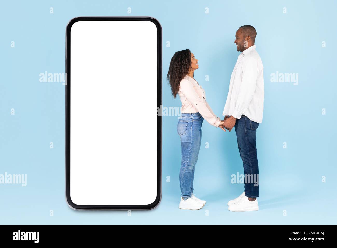 Loving black couple standing near large mobile phone with blank screen ...