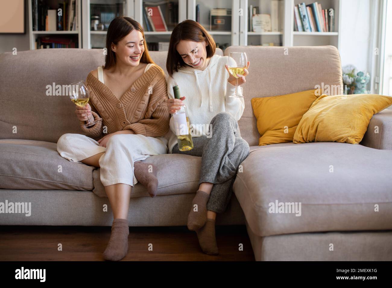 Laughing european millennial ladies in sweaters with glasses of wine ...