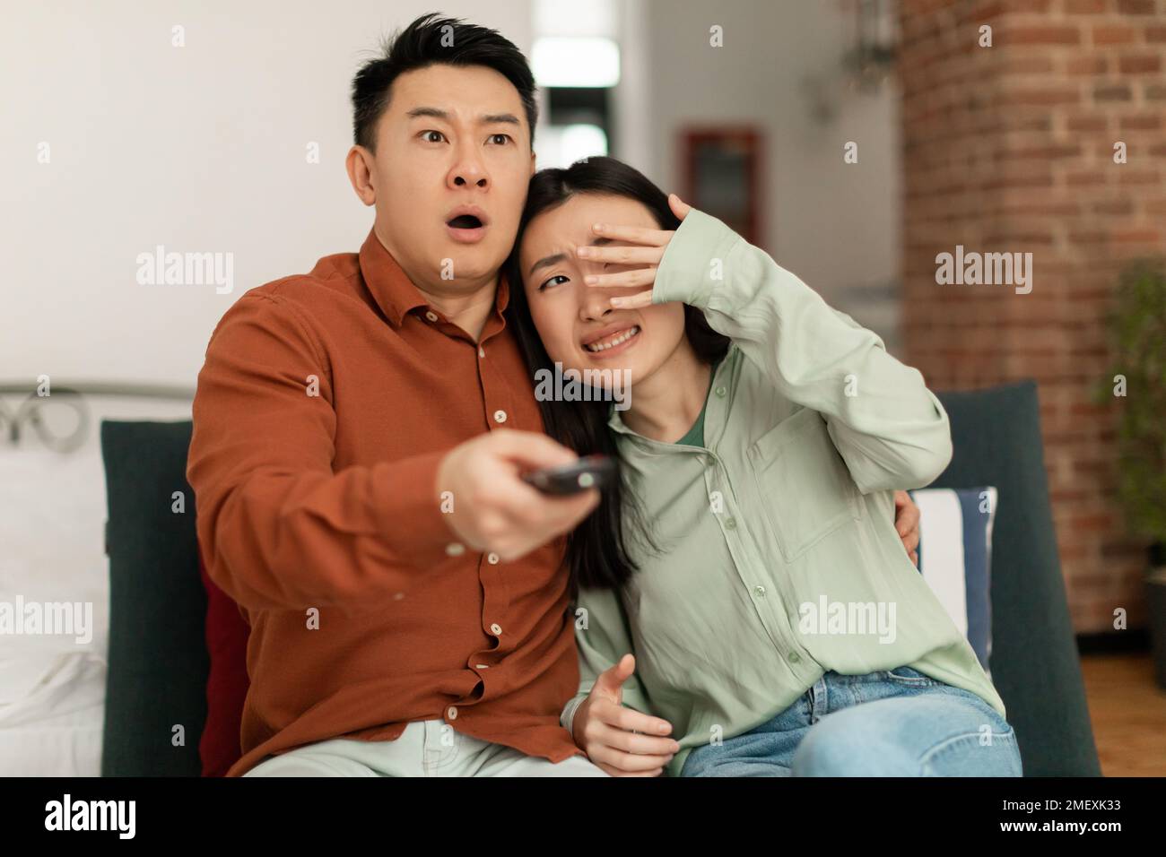 Shocked korean couple watching horror movie, man holding television ...