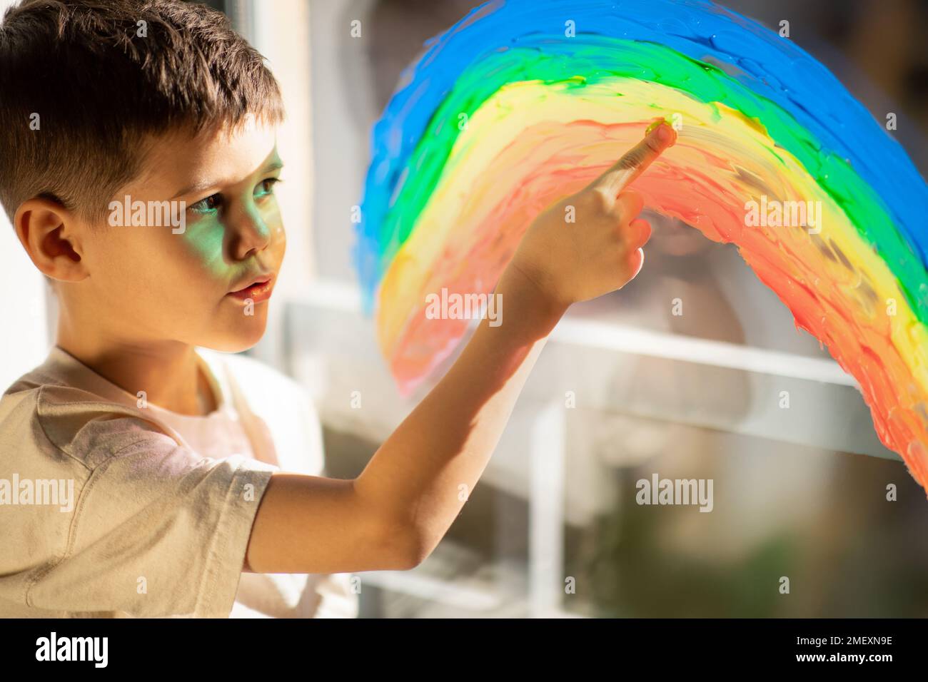 Serious little boy draws rainbow on window with hand, dream, think in ...