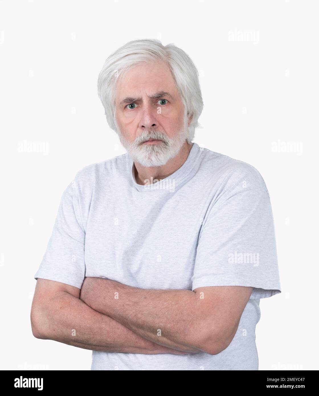 Vertical shot of an angry old man with white hair with his arms crossed on a white background ...