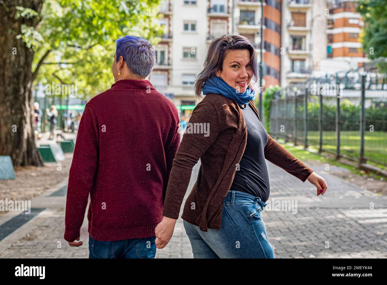 Back view of two friends walking in the park. She turns around to look ...