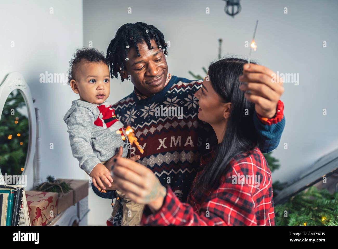 Smiling multiracial parents and their toddler with Christmas sparkling ...
