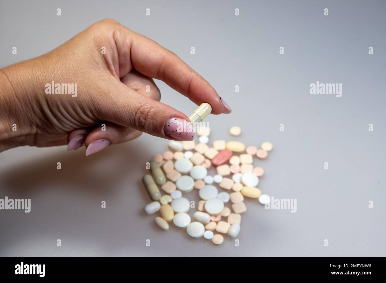 A woman's hand holding a medicine pill, and many pills in defocused ...