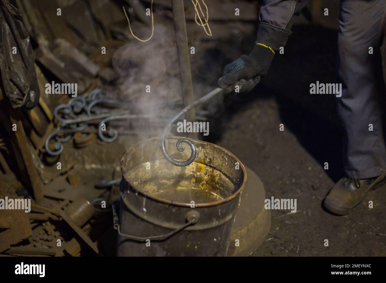 Blacksmith quenching hot iron part Stock Photo - Alamy