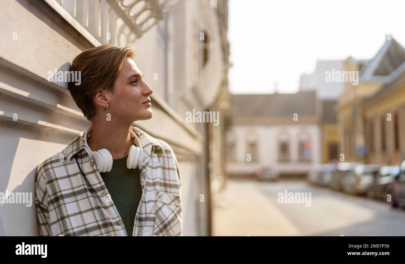 Short red hair woman standing on street with headphones on her neck ...