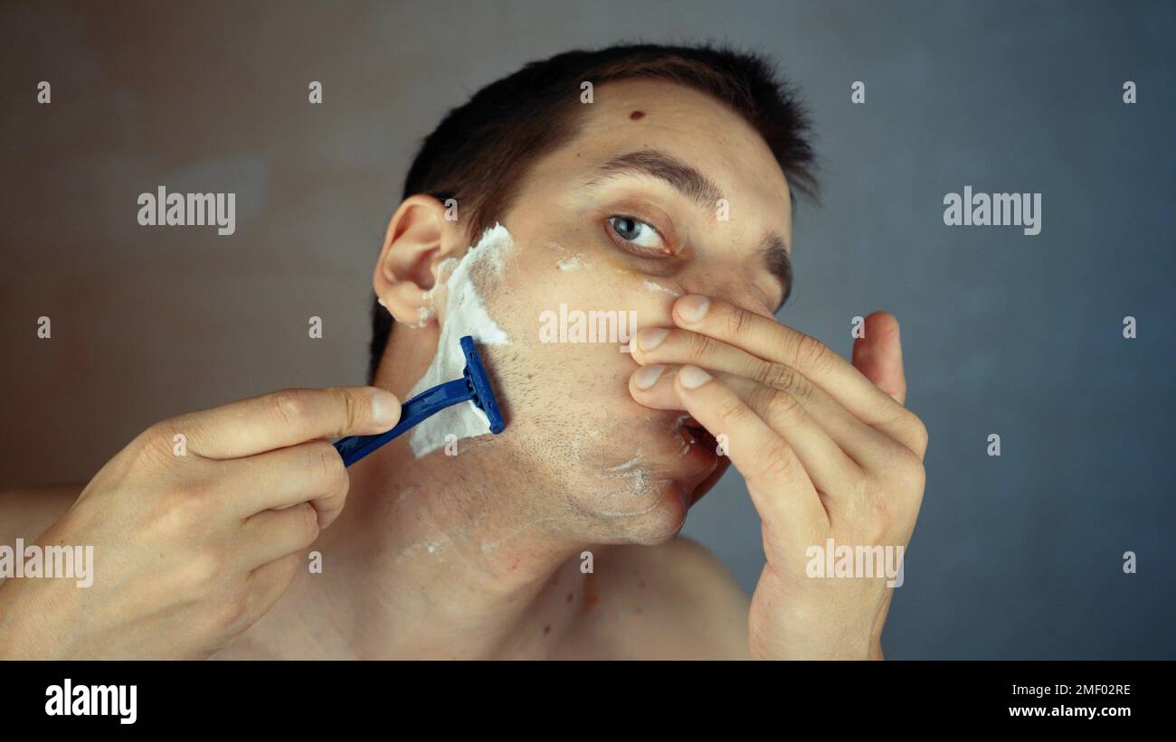 Young man is shaving using disposable razor in bathroom, closeup. Daily ...
