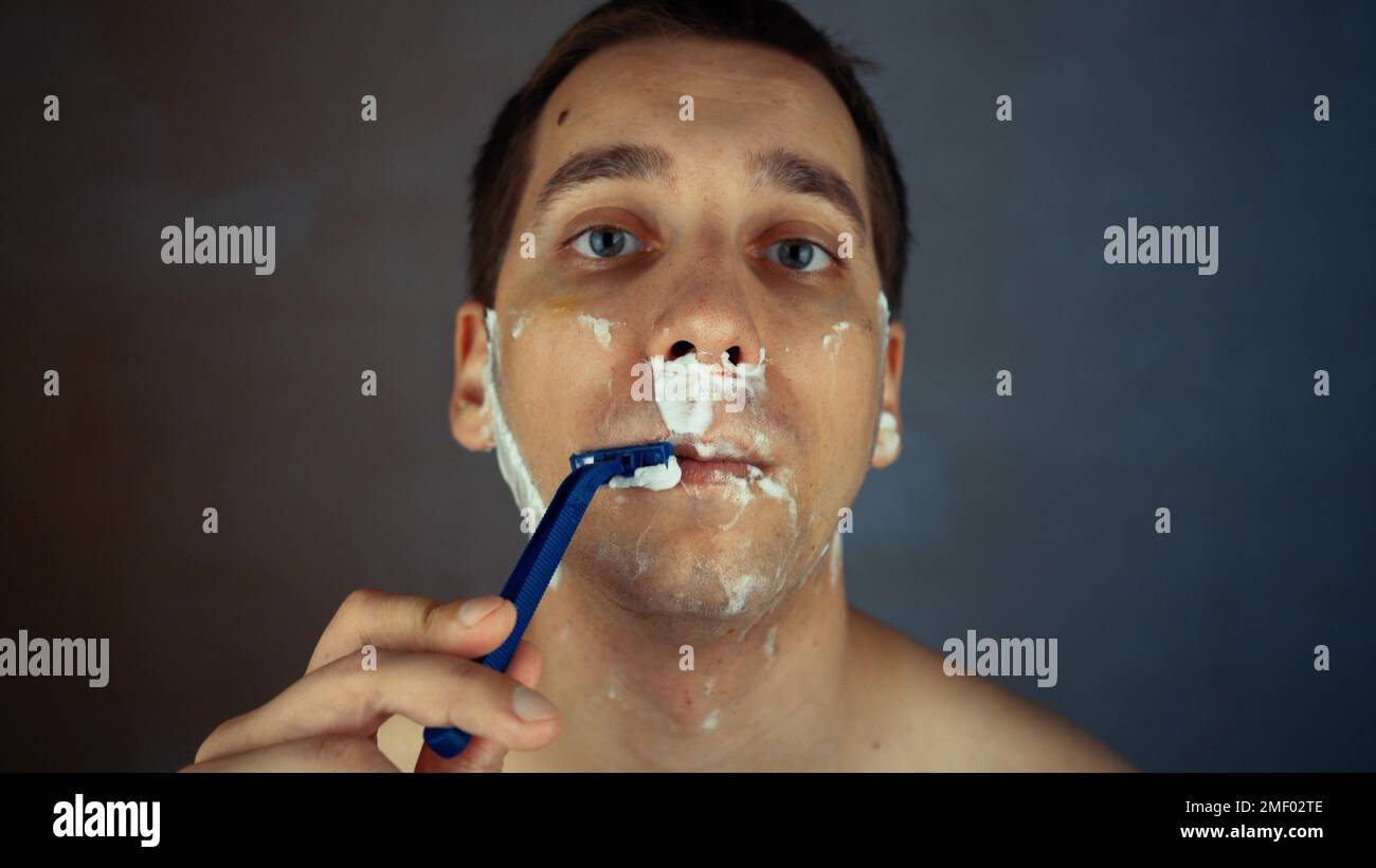 Young man is shaving using disposable razor in bathroom, closeup. Daily ...