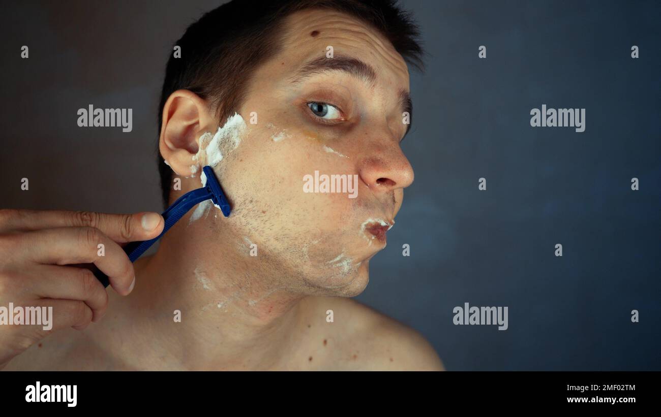 Young man is shaving using disposable razor in bathroom, closeup. Daily ...