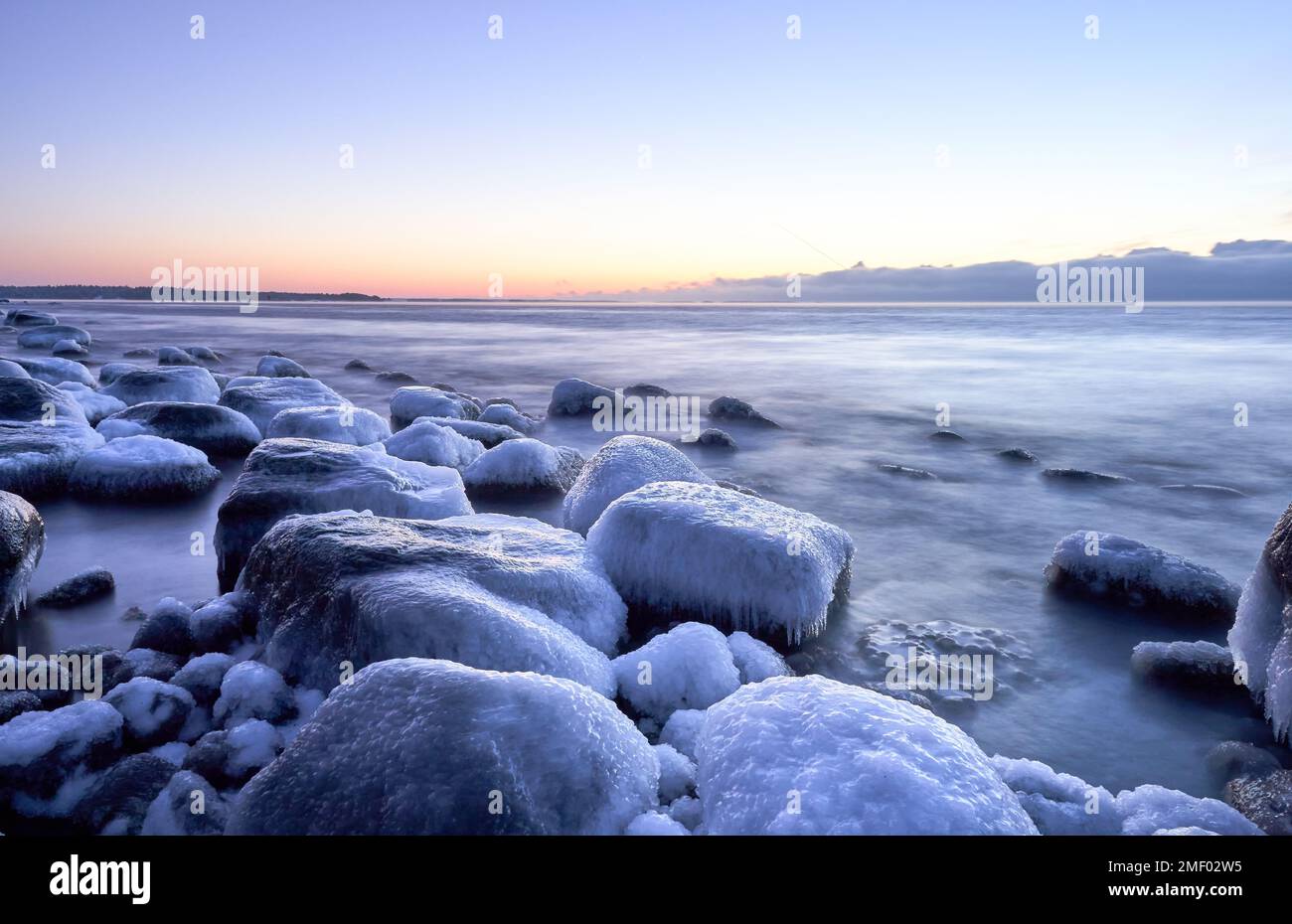 A high angle shot of frozen rocks covered in snow near a frozen lake ...