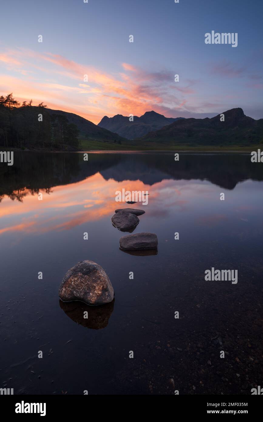 Beautiful sunset sky reflecting in perfectly still water with rocks in ...