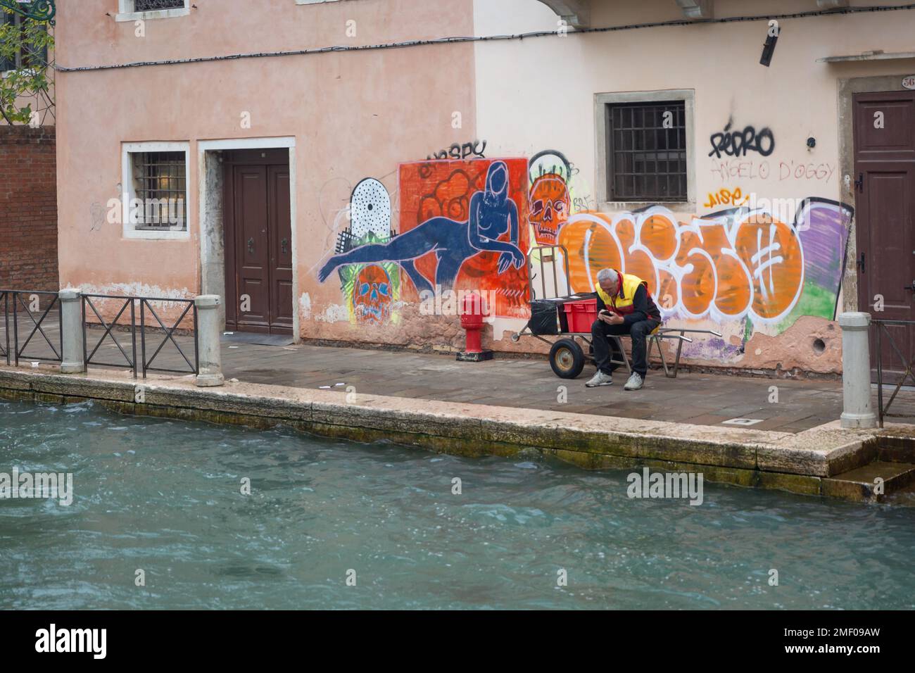 Man sitting in front of graffiti-painted walls along canal in Venice ...