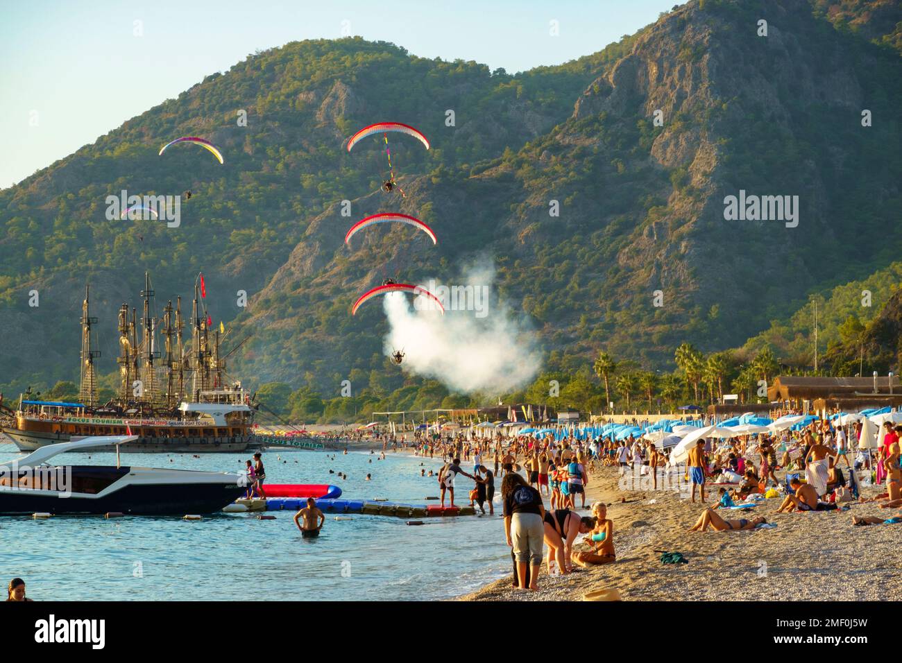 Paramotor pilots flying over boats and beachgoers in Belcekiz Beach ...